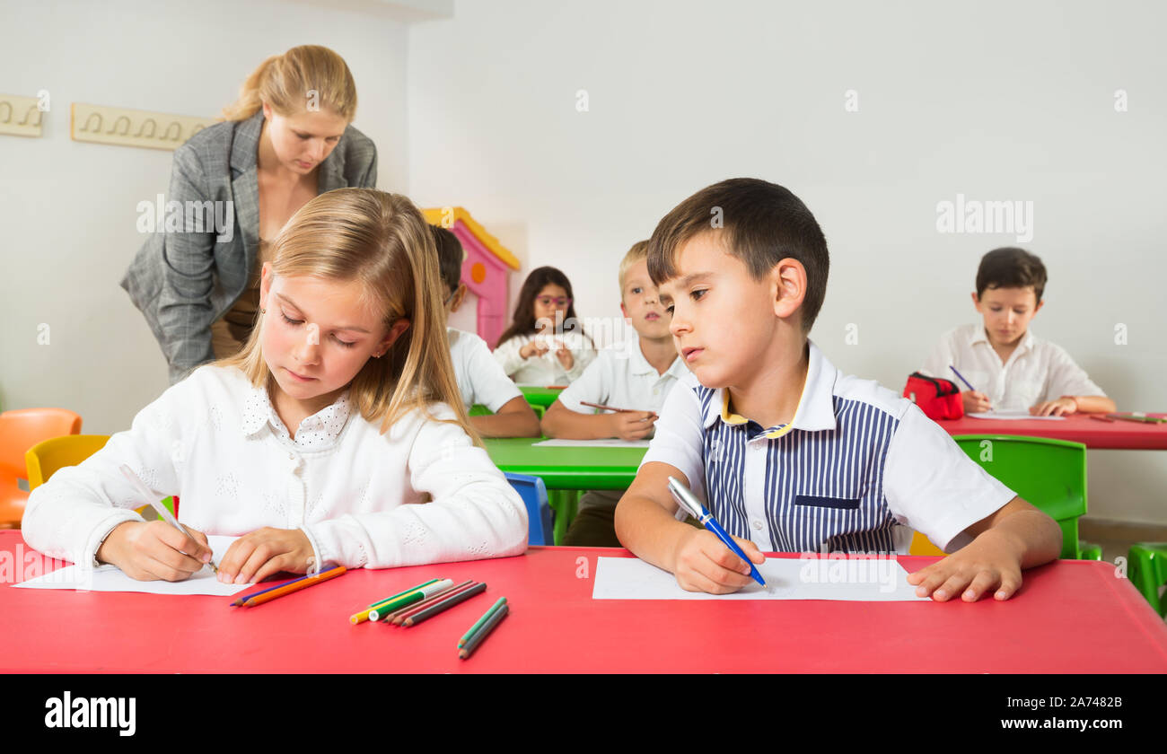 Group of school kids with pens and notebooks studying at classroom with ...