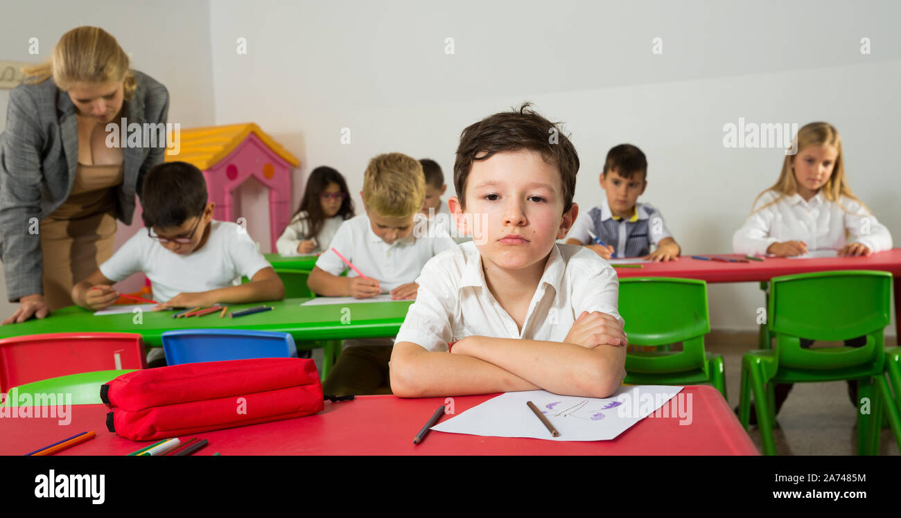 Portrait of upset boy in schoolroom on background with pupils studying ...