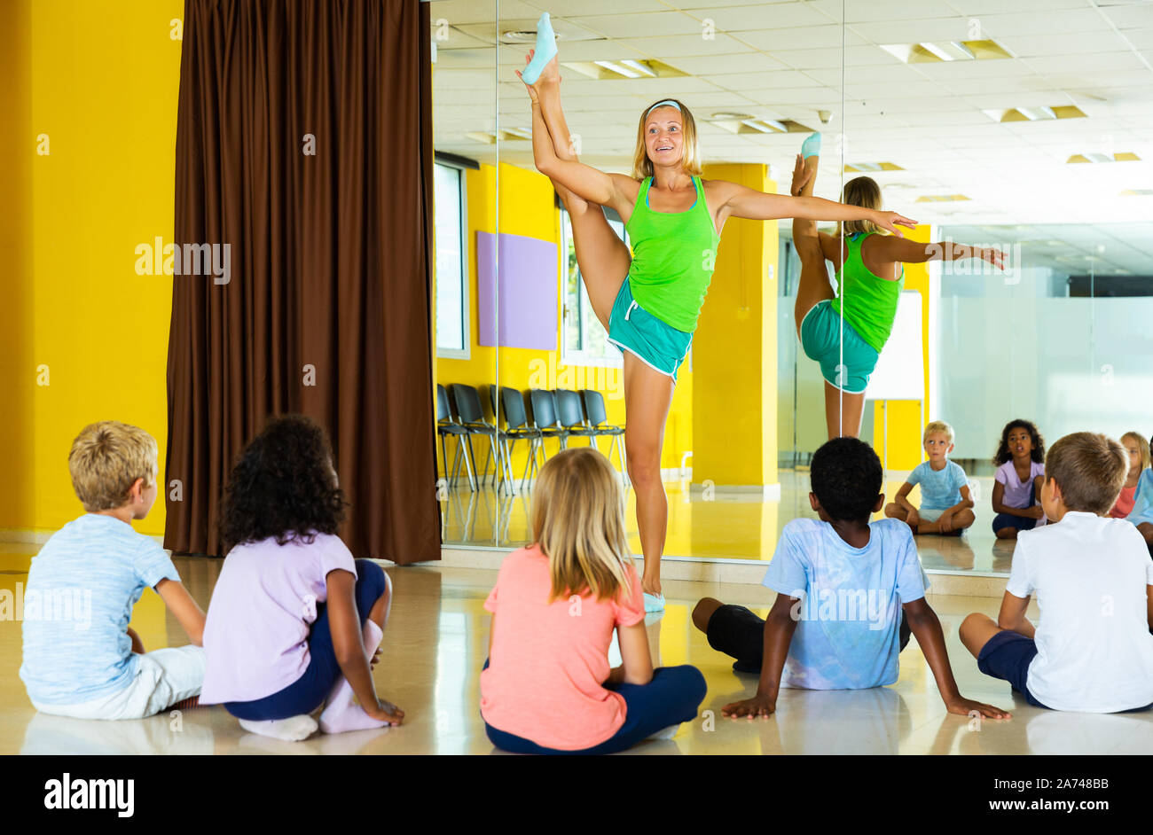 Young dance teacher giving children dance class, showing movements in ...