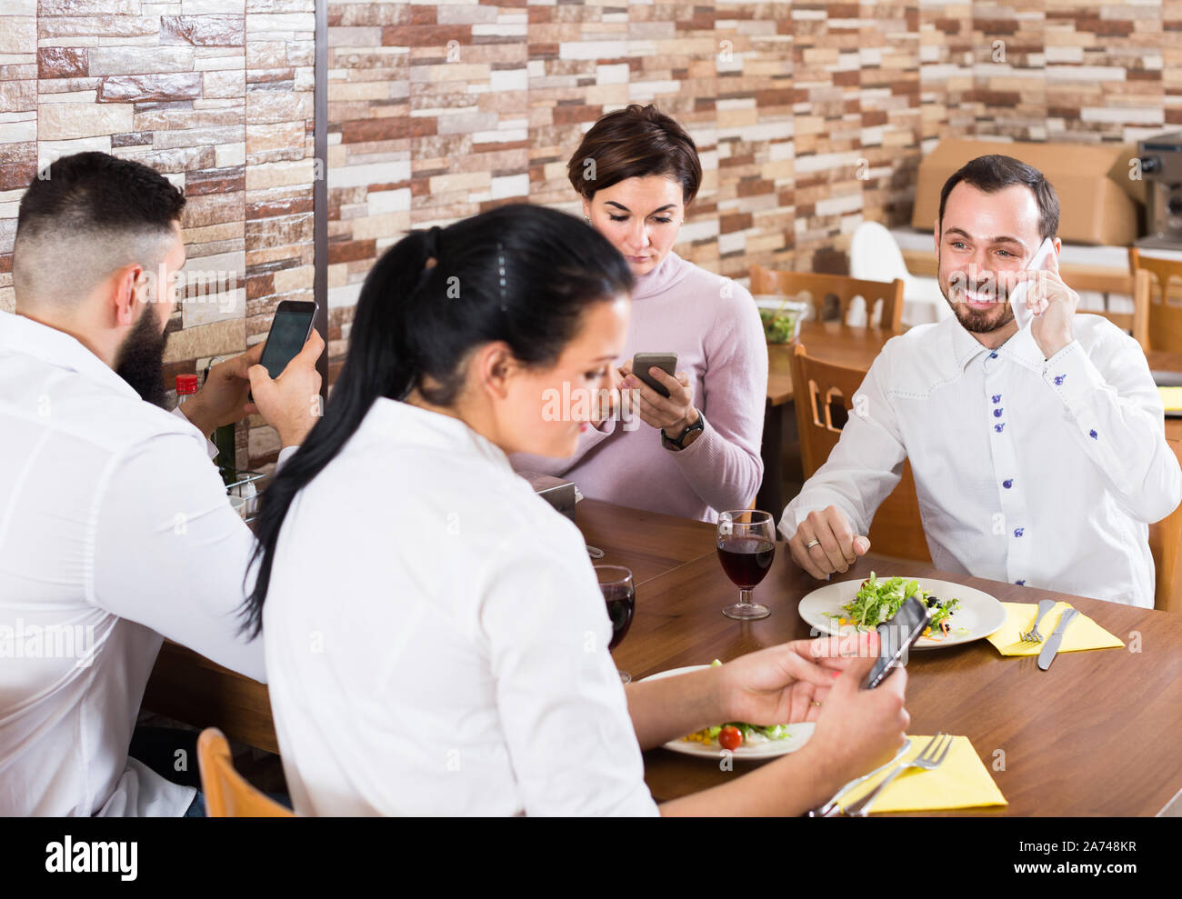 group of serious friends busy with phone ignoring dinner in restaurant ...