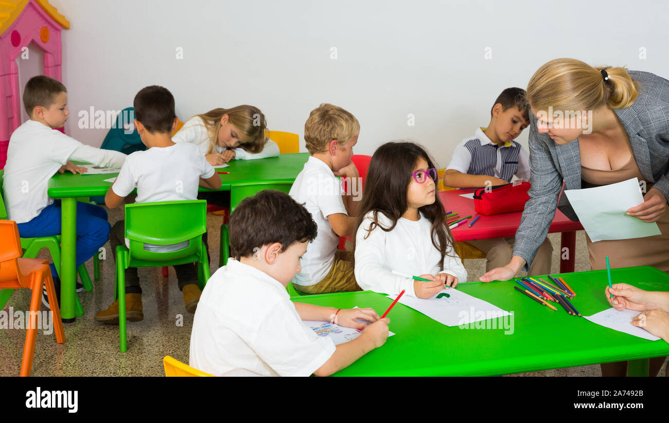 Female teacher helping schoolchildren doing their task in classroom ...