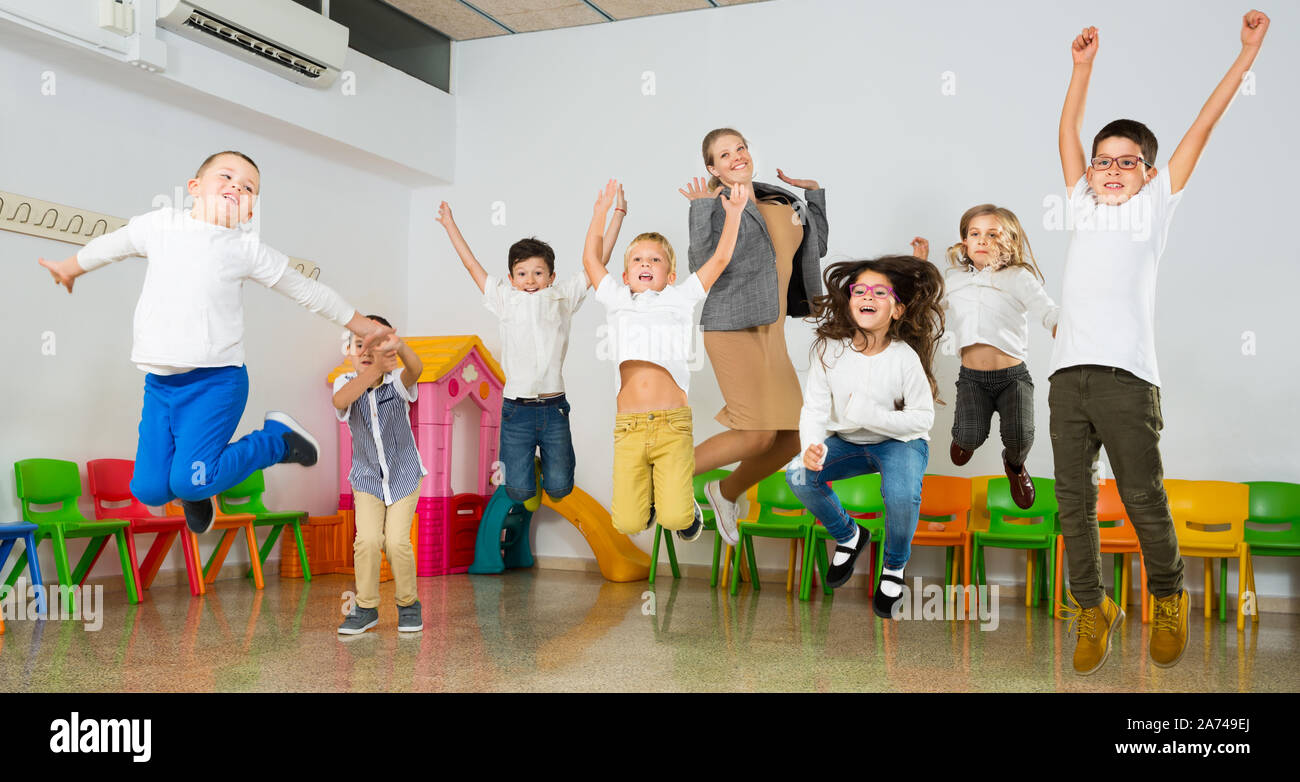 Group of happy cheerful children with their female teacher jumping ...