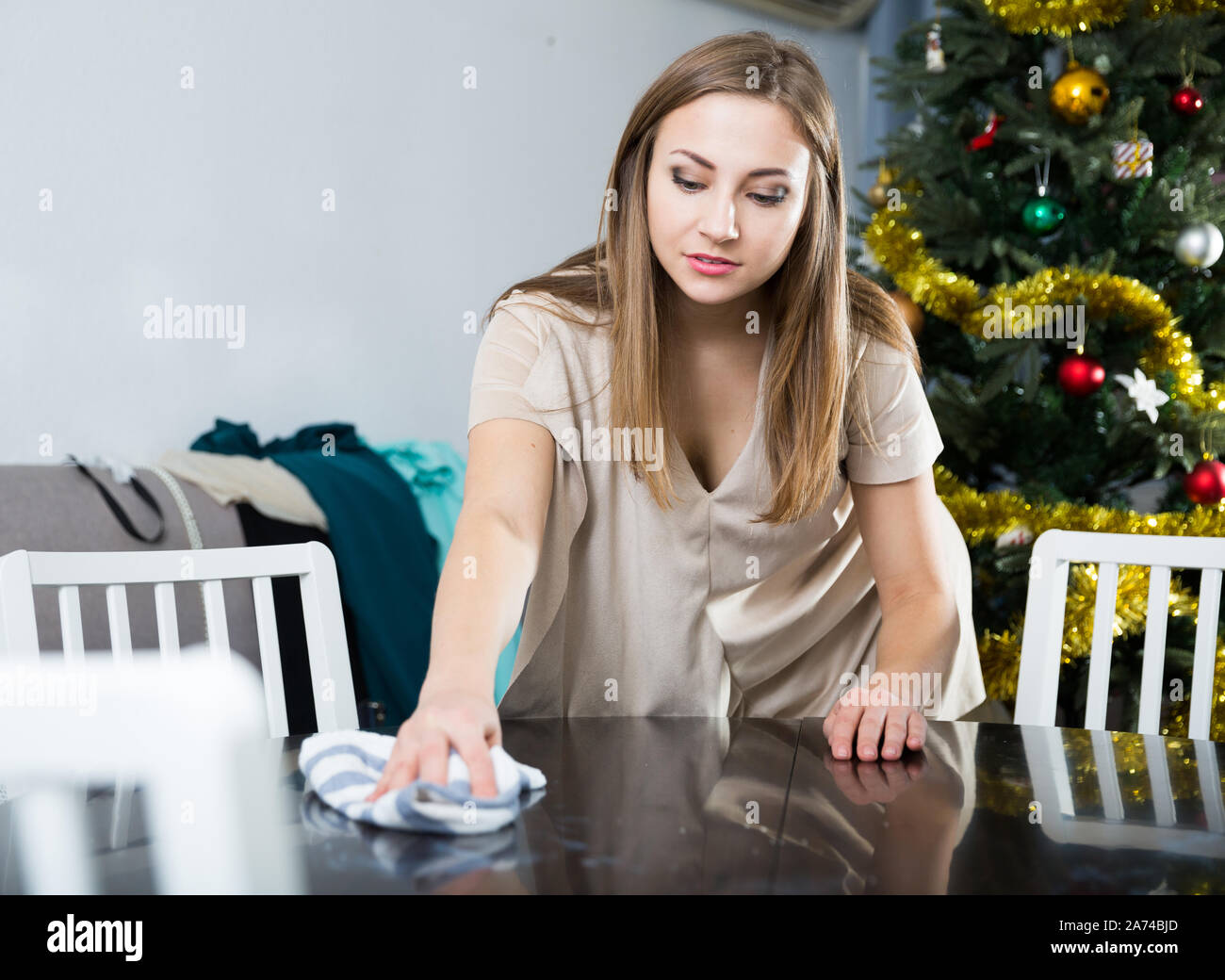 Portrait of attractive young woman wiping table before Christmas ...