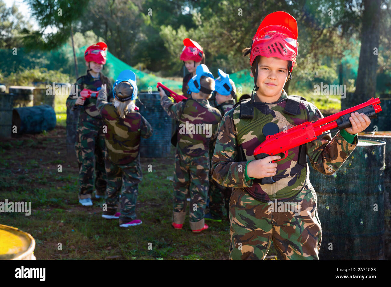 Happy cheerful boy paintball player in camouflage standing with gun ...