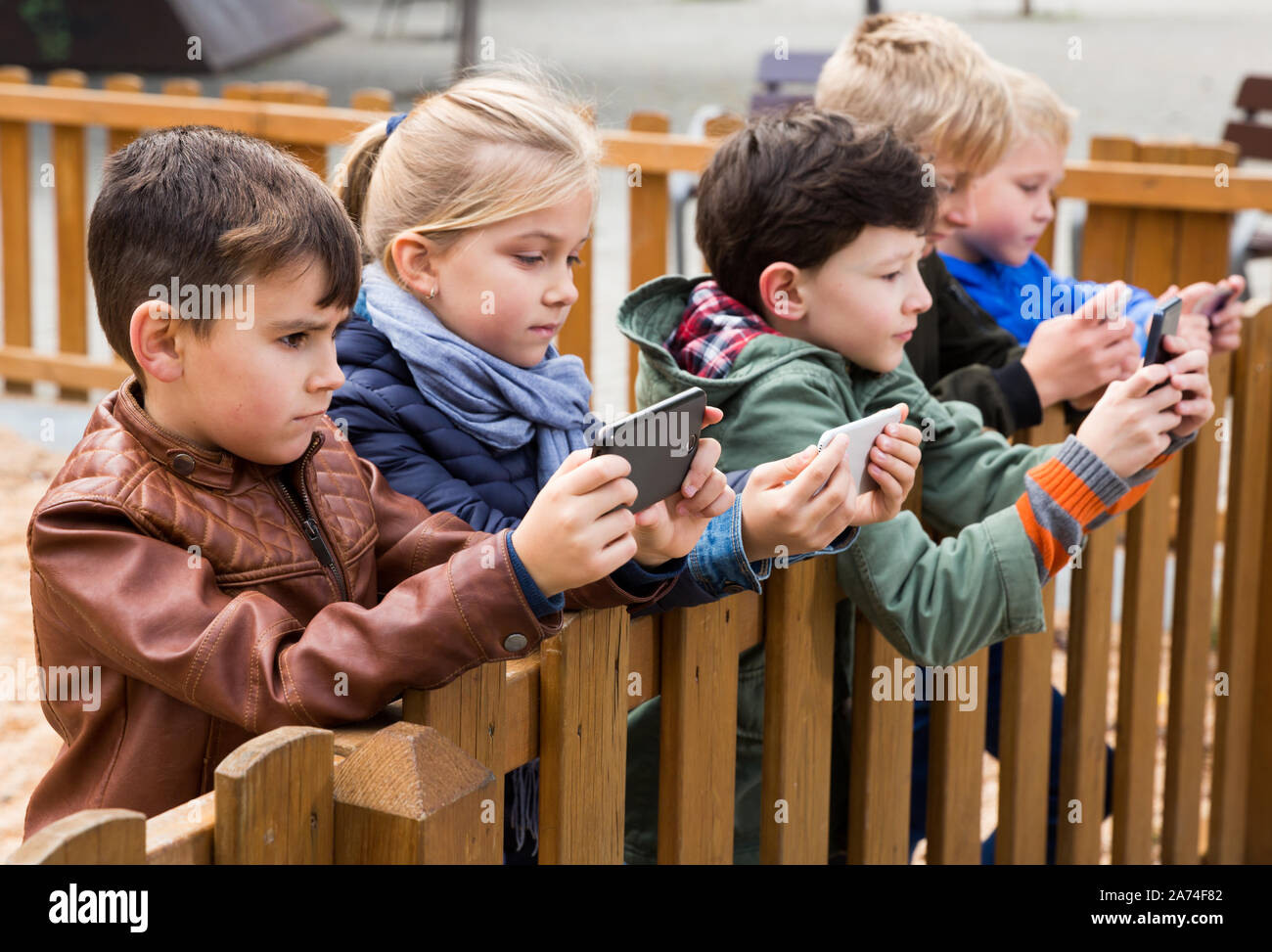 Interested kids playing with smartphones while standing near wooden ...