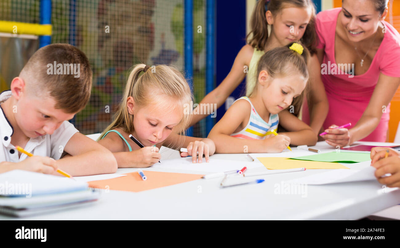 Glad children drawing on lesson in elementary school class with help of ...