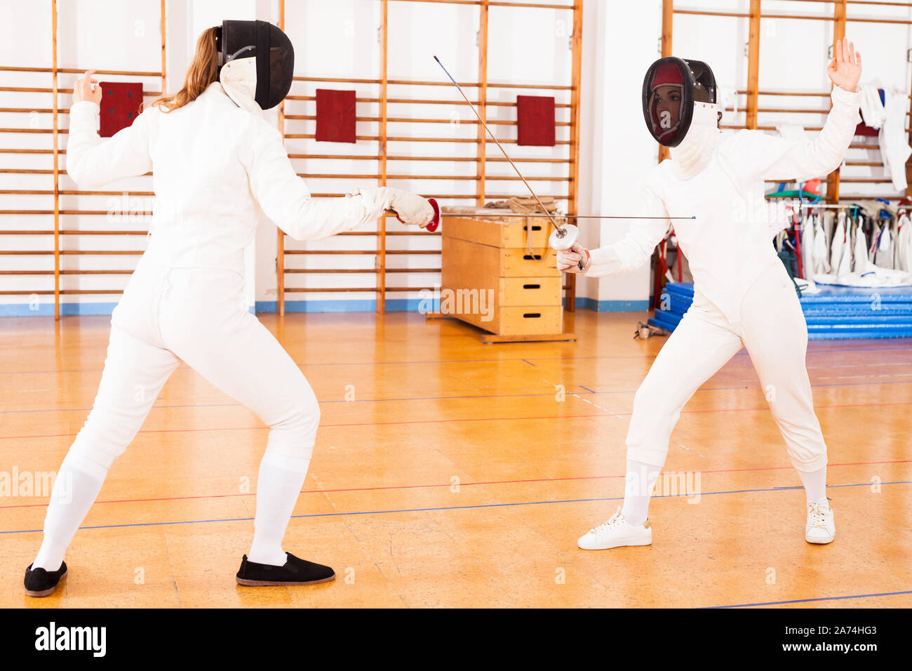 active young female athletes in uniform practicing movements at fencing ...