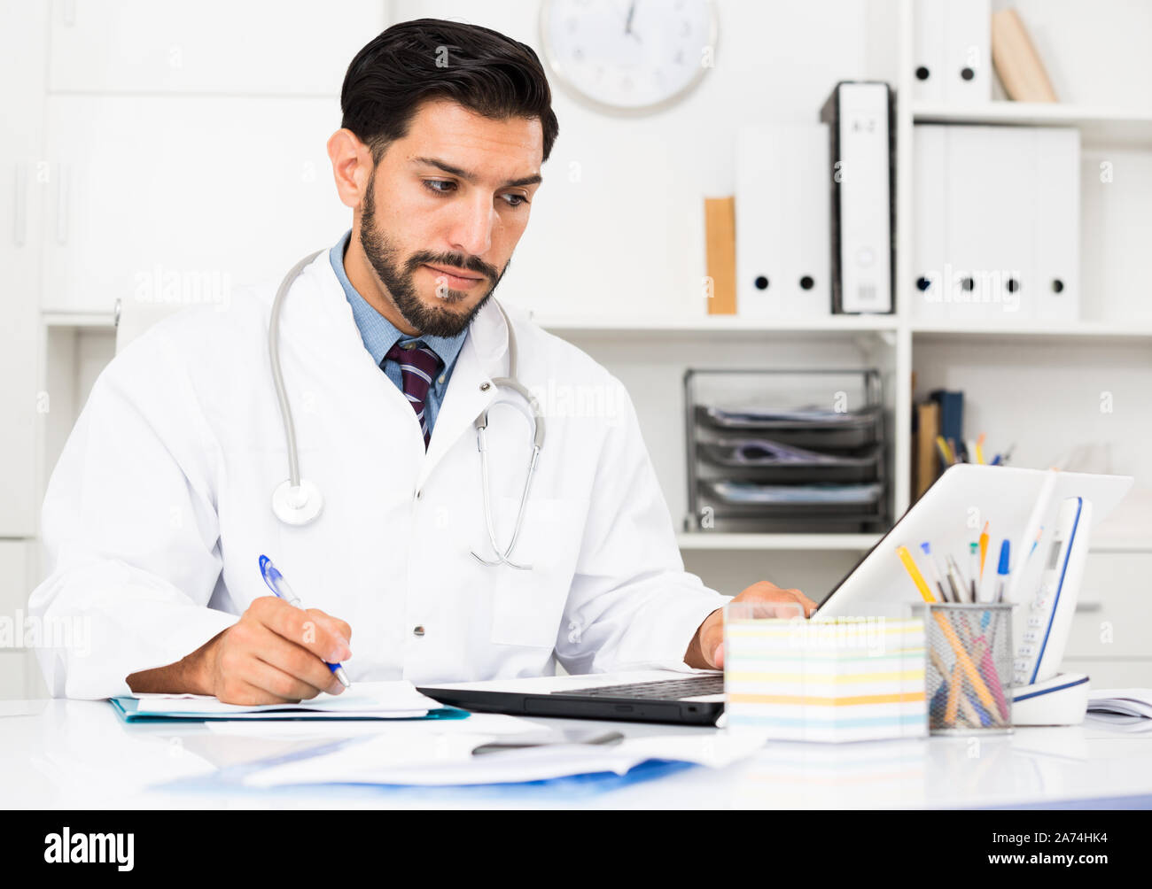 Spanish man doctor is working with documents behind laptop in his ...