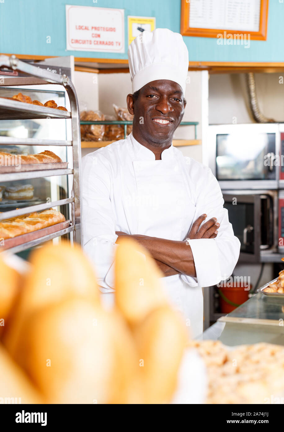 Smiling African-American baker wearing white uniform standing with arms ...