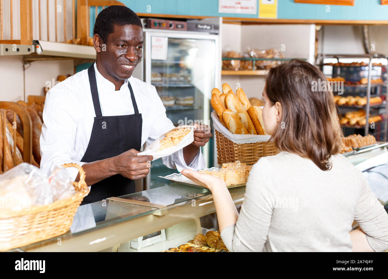 Polite male baker working behind counter in store of his bakery ...