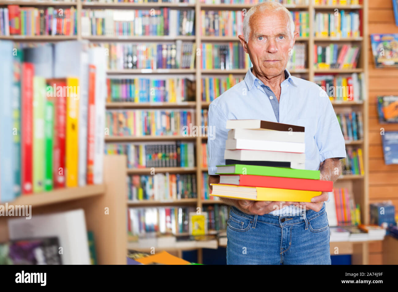 Portrait of calm older man standing in library with pile of books in ...