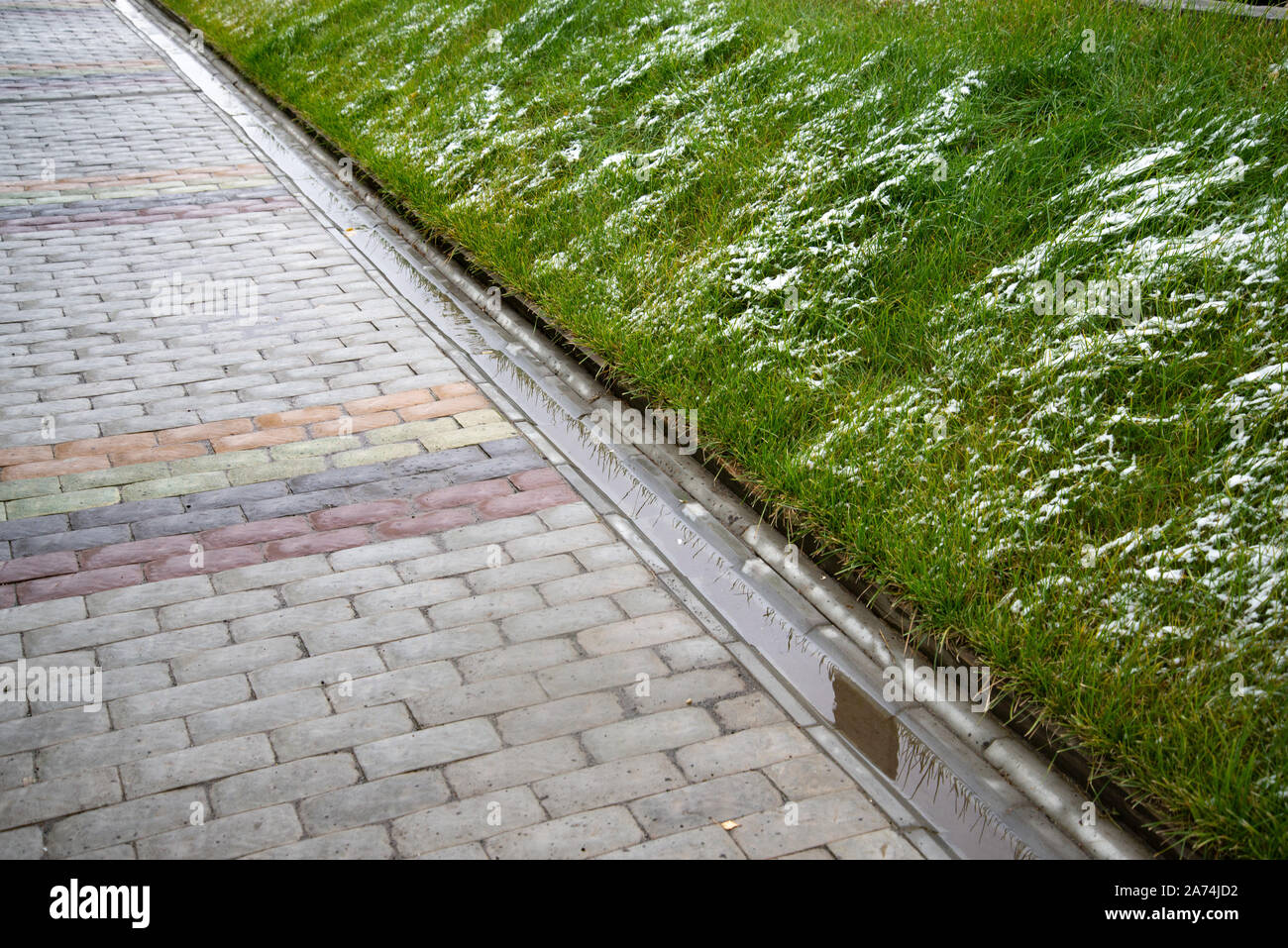 Wet tiled sidewalk at the beginning of winter. Lawn with green grass ...