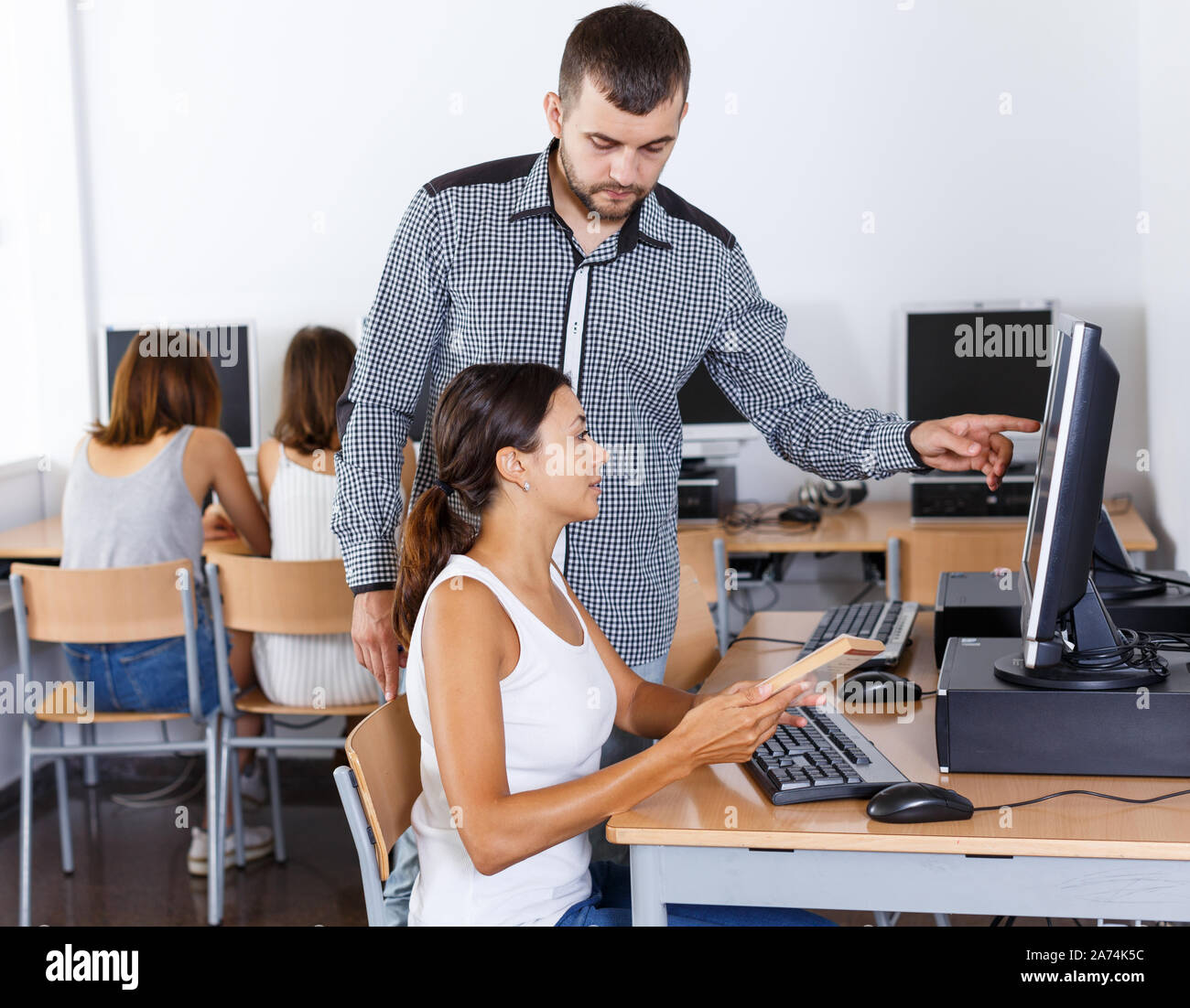 Teacher helping young female student in computer class in university ...