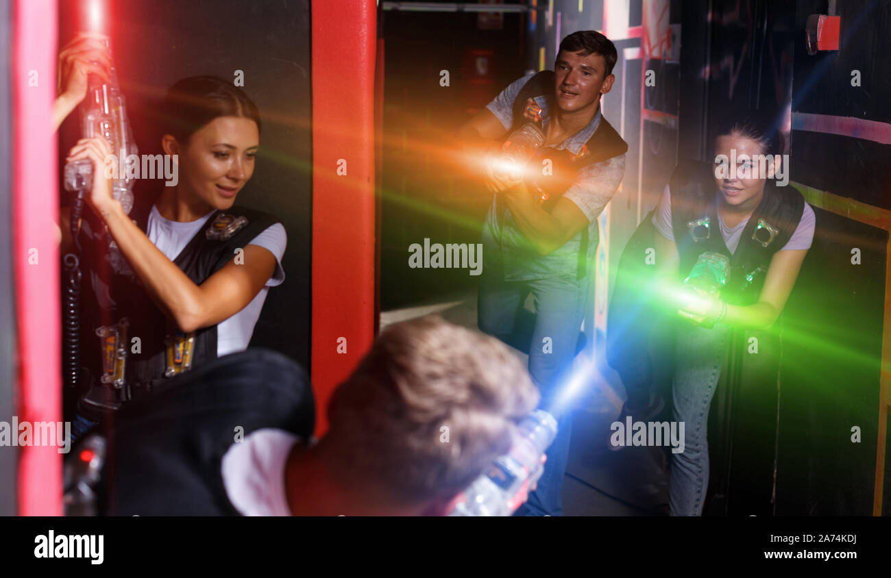 Group of young people playing laser tag game with laser guns in dark ...