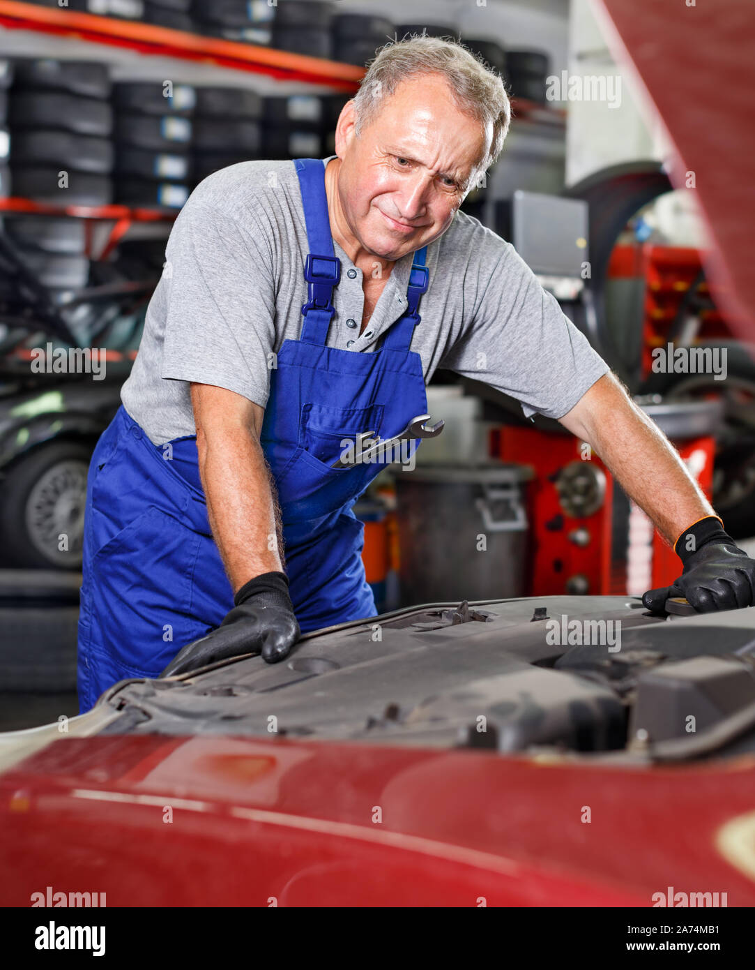 Skilled mature car mechanician changing motor oil in vehicle in an auto ...