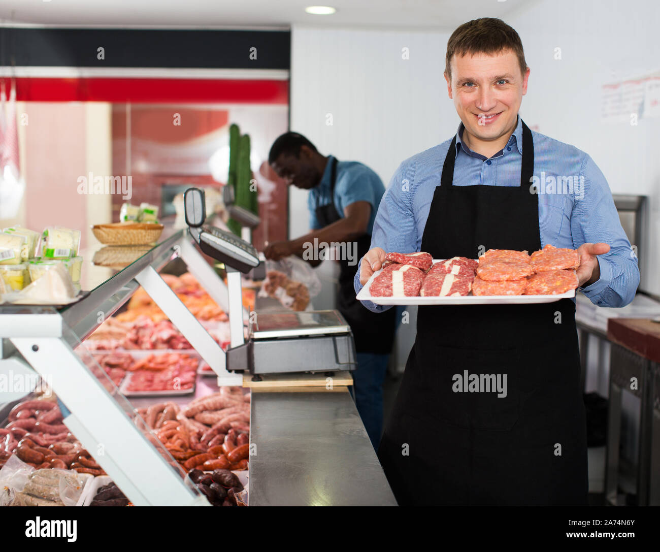 Professional smiling butcher arranging meat products in display case of ...