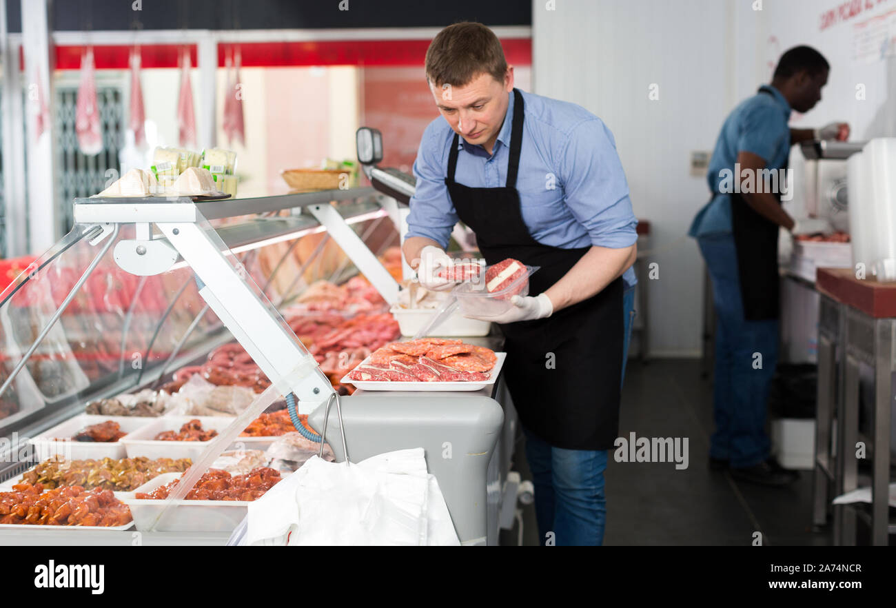 Two professional butchers arranging meat products in display case of ...