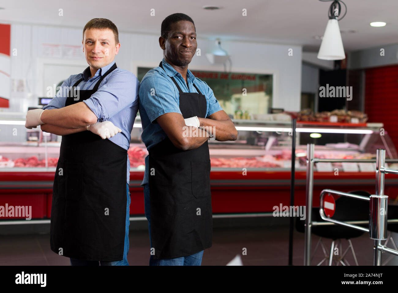 Two confident professional butchers standing in hall of butcher shop ...