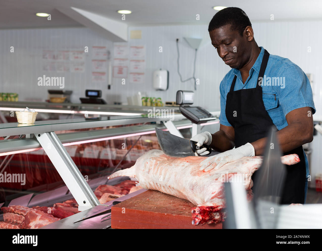 African American male butcher cutting lamb carcass in butcher shop ...