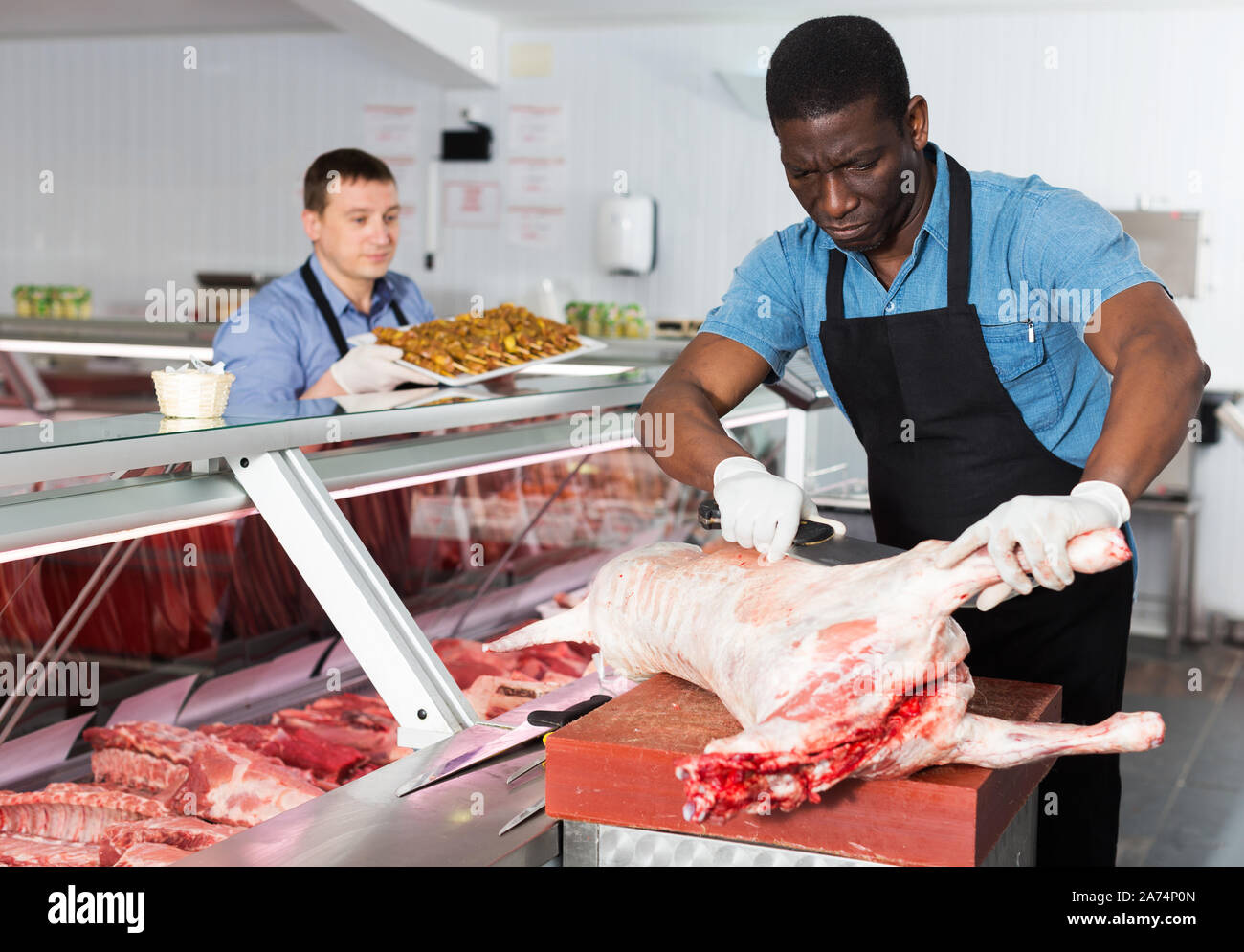 African American male butcher processing carcase of young lamb for sale ...