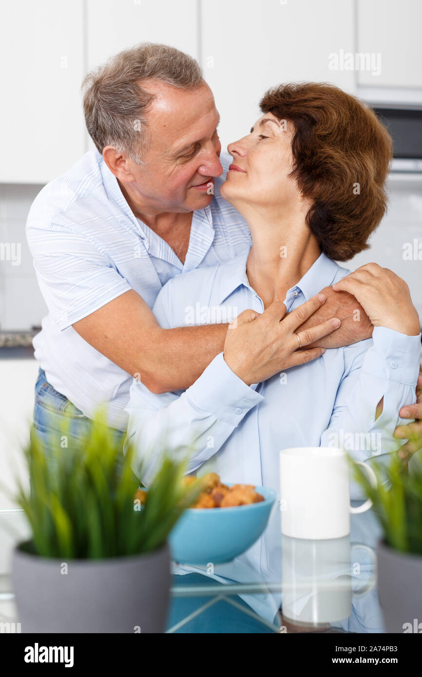 Portrait of happy mature couple hugging near kitchen table before ...