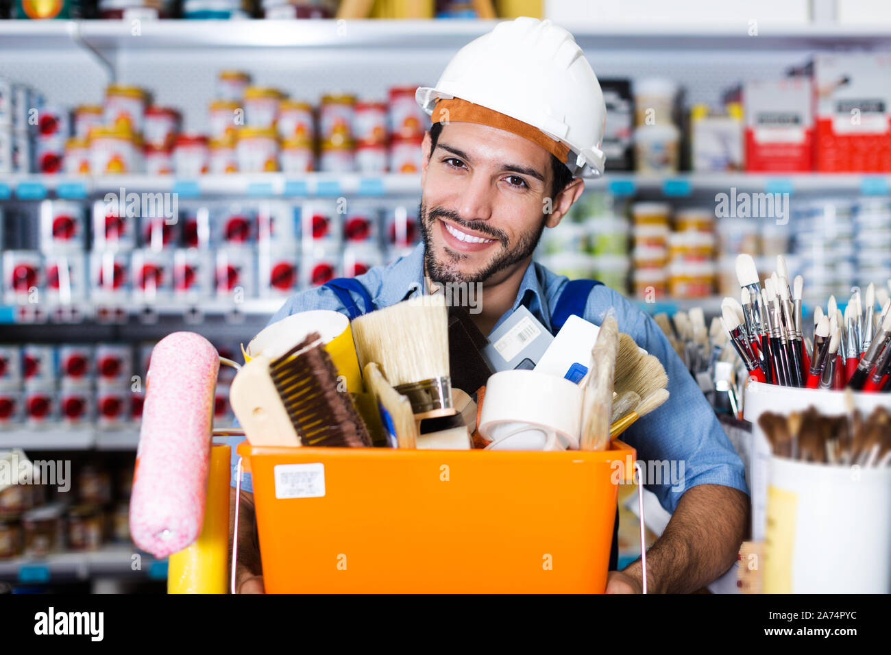 portrait of satisfied young foreman standing near racks in paint store ...