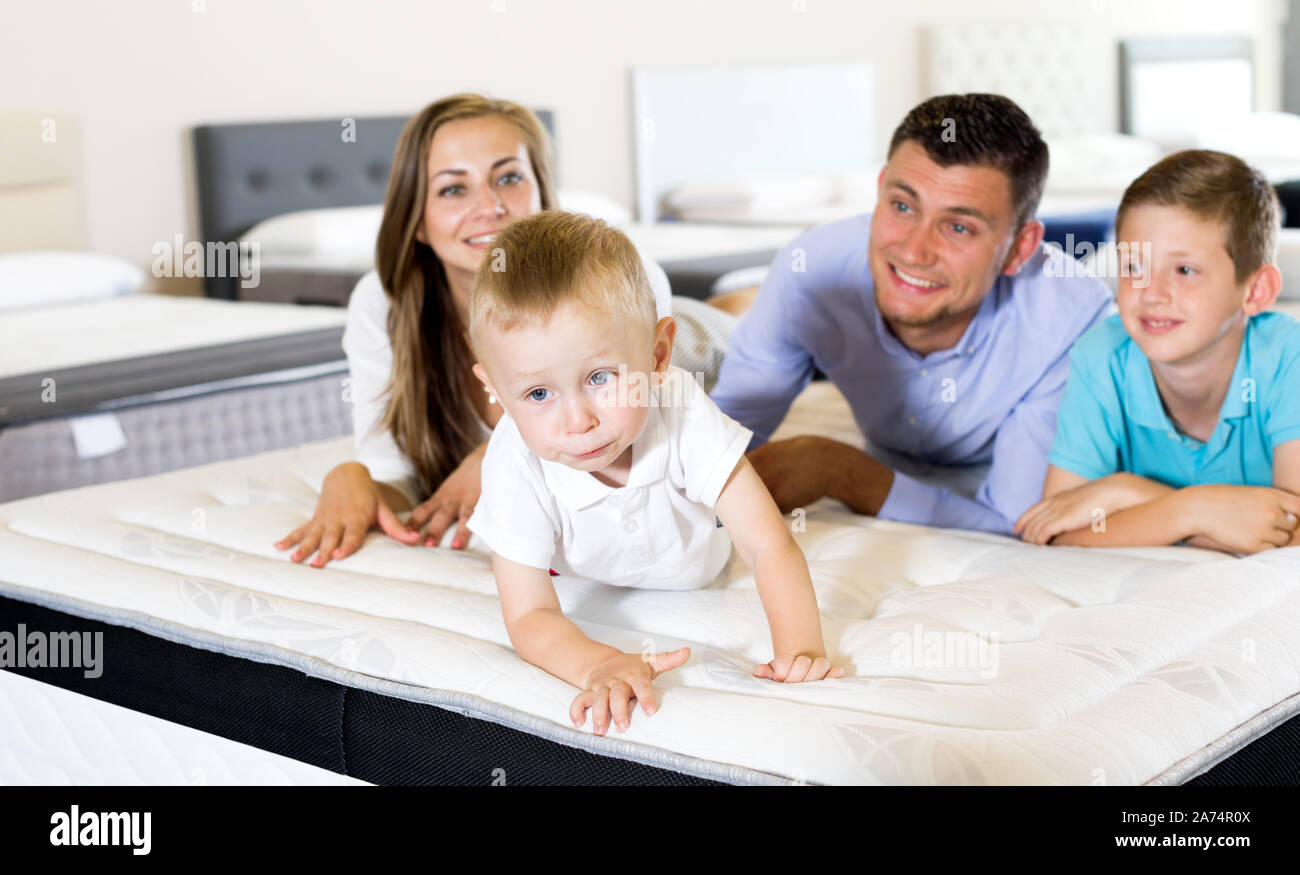 Little glad boy with brother and parents testing mattress in store ...
