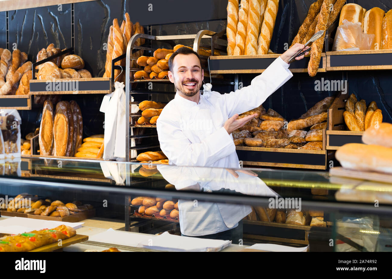 Happy European Male Shop Assistant Demonstrating Delicious Loaves Of