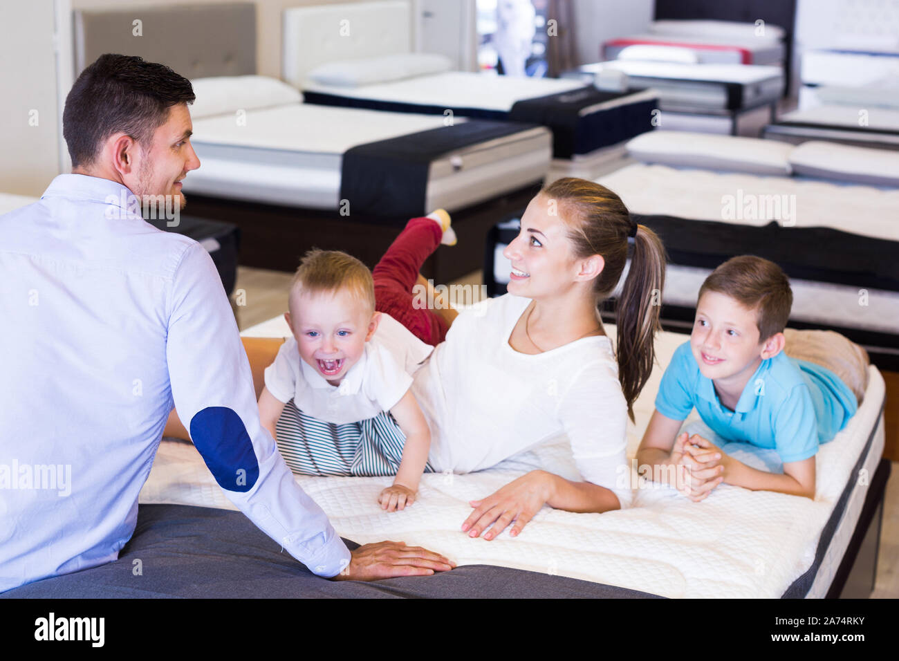 Happy parents with two sons testing mattress in store, looking at each ...
