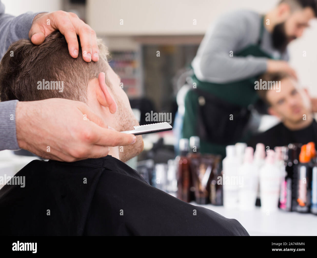 Positive guy stylist creating new shape for beard of client at ...