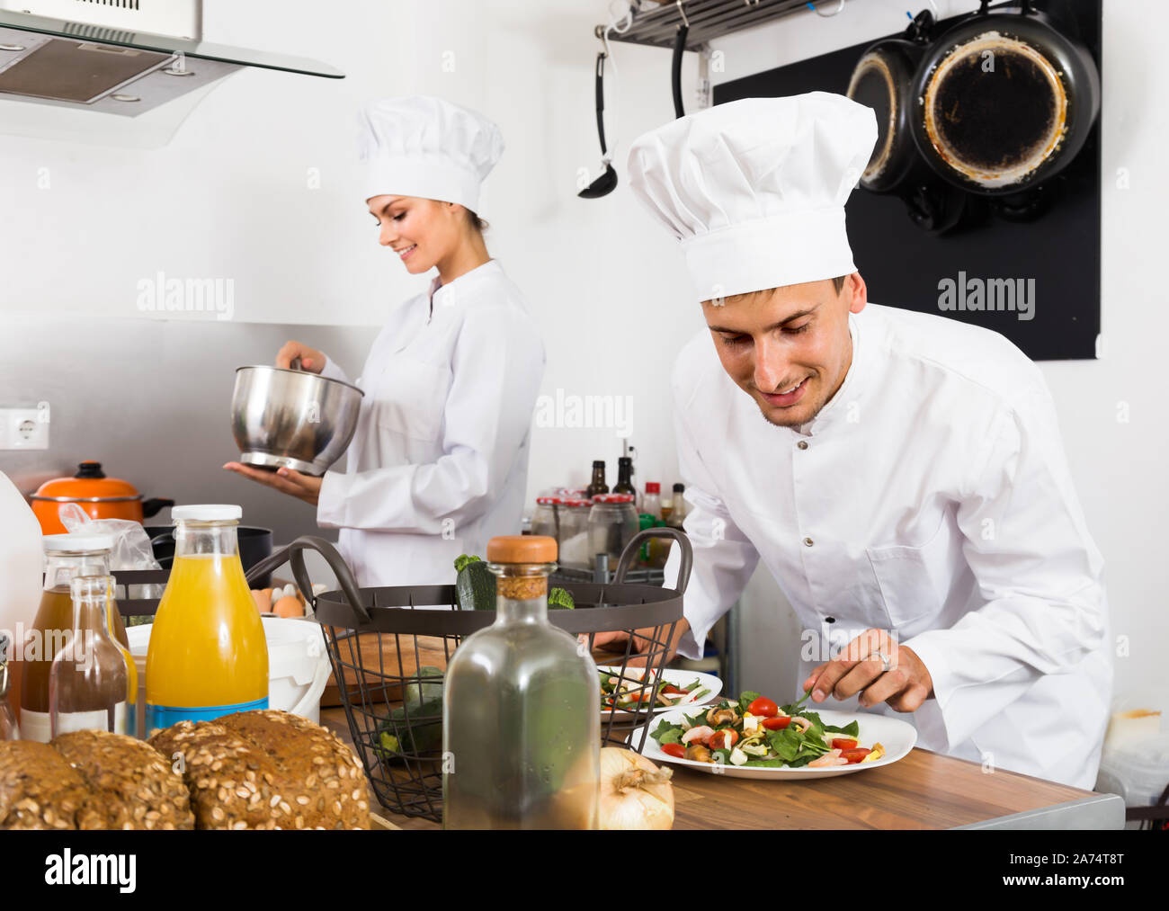 Two positive female and male young cooks wearing uniform working on ...