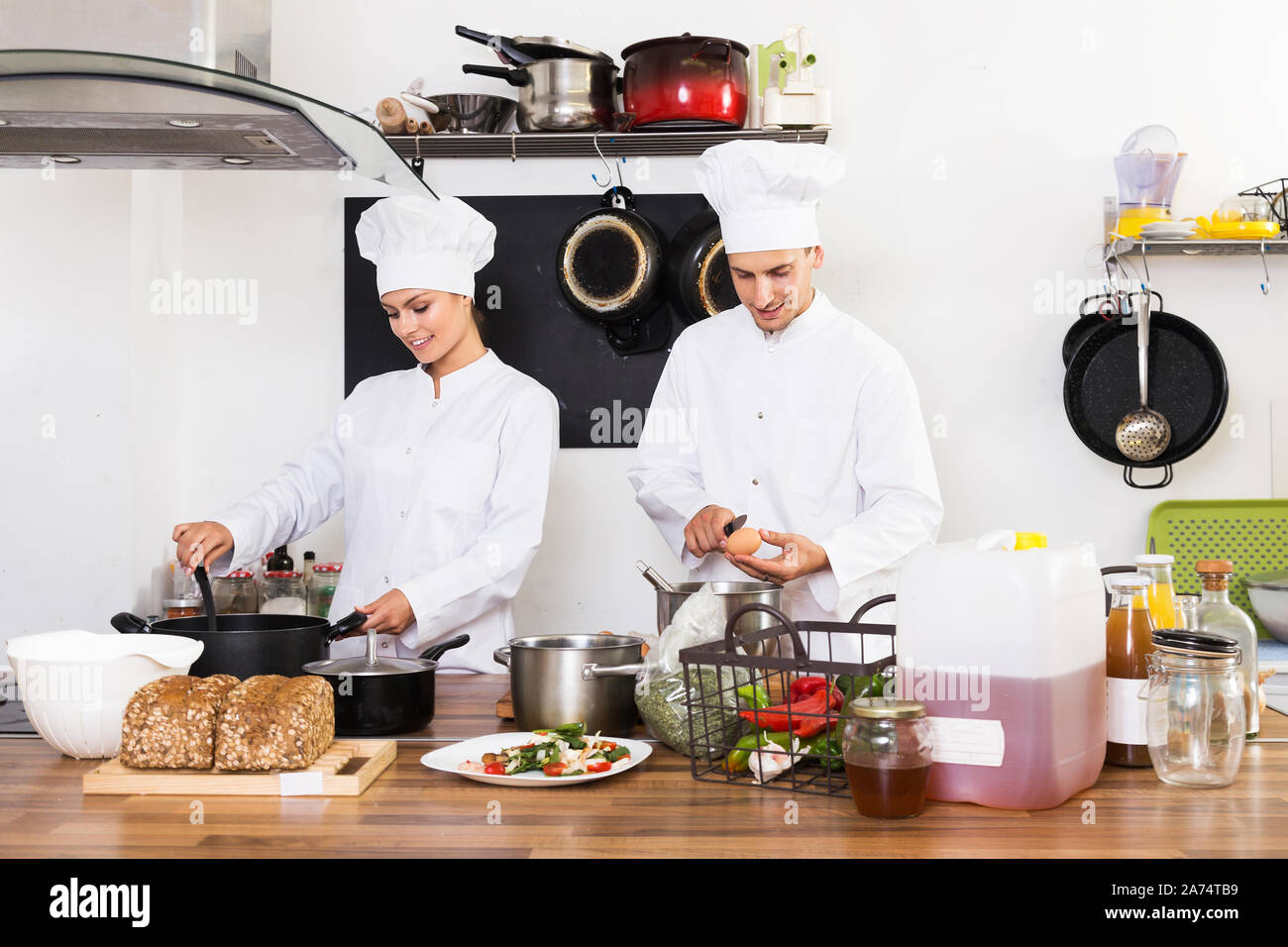 Two positive young man and woman chefs cooking food at restaurant's ...