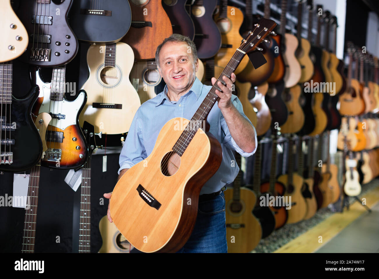 Adult glad cheerful positive guitarist is standing with acoustic guitar ...