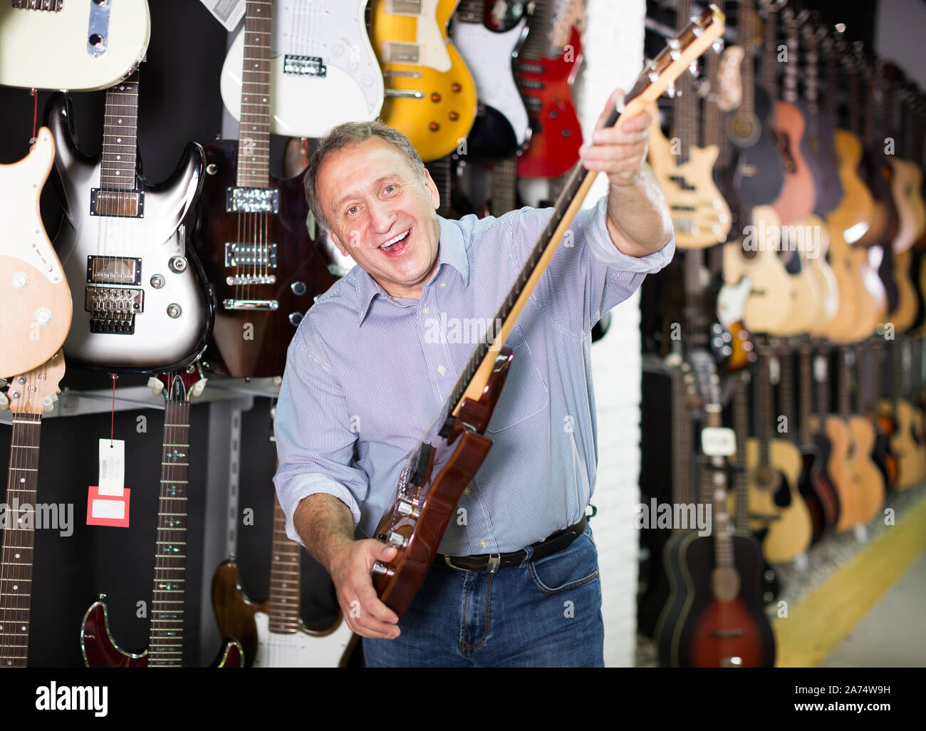 Smiling musician demonstrating an electric guitar in a music store ...