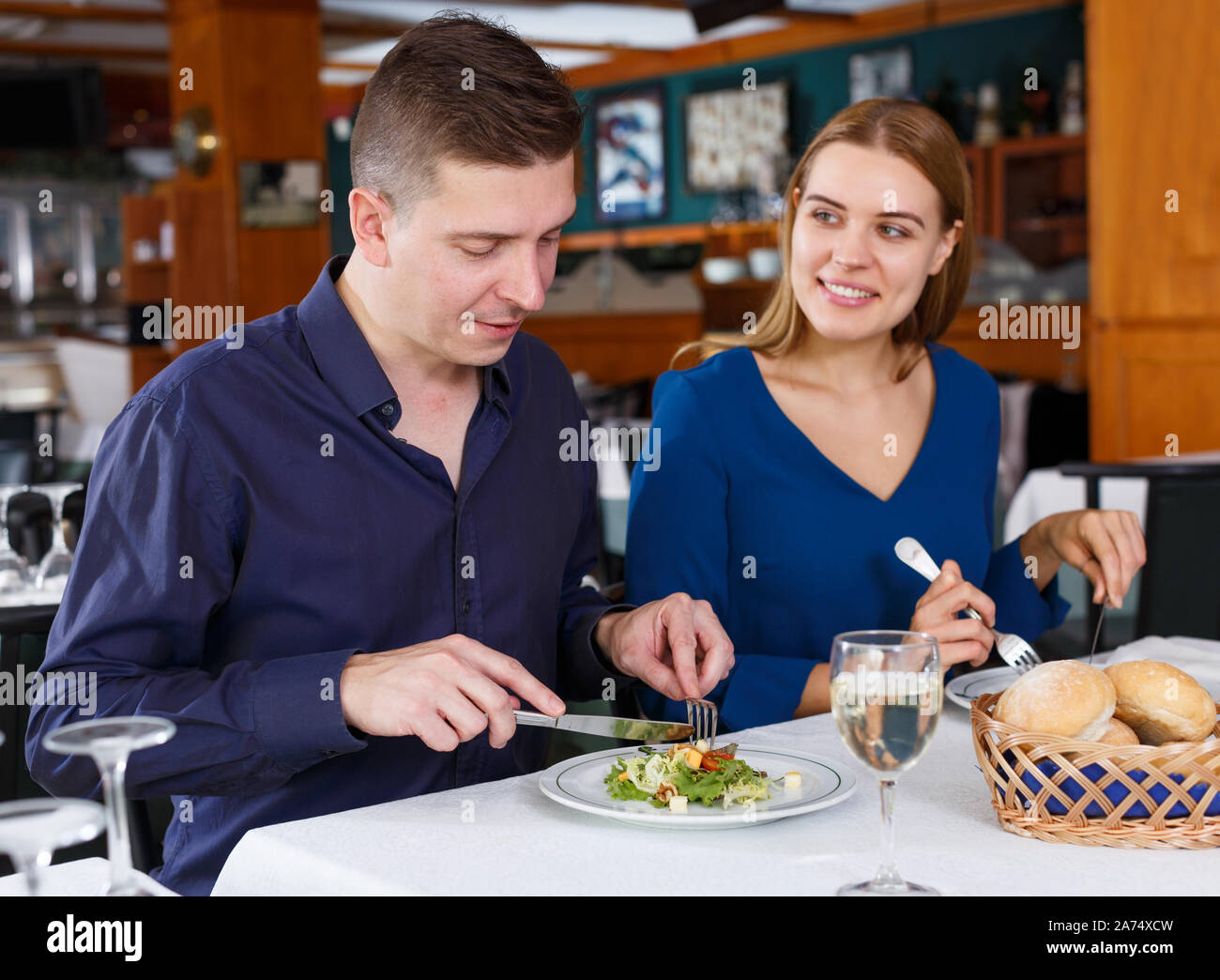Happy couple on date eating salad and drinking white wine in restaurant ...