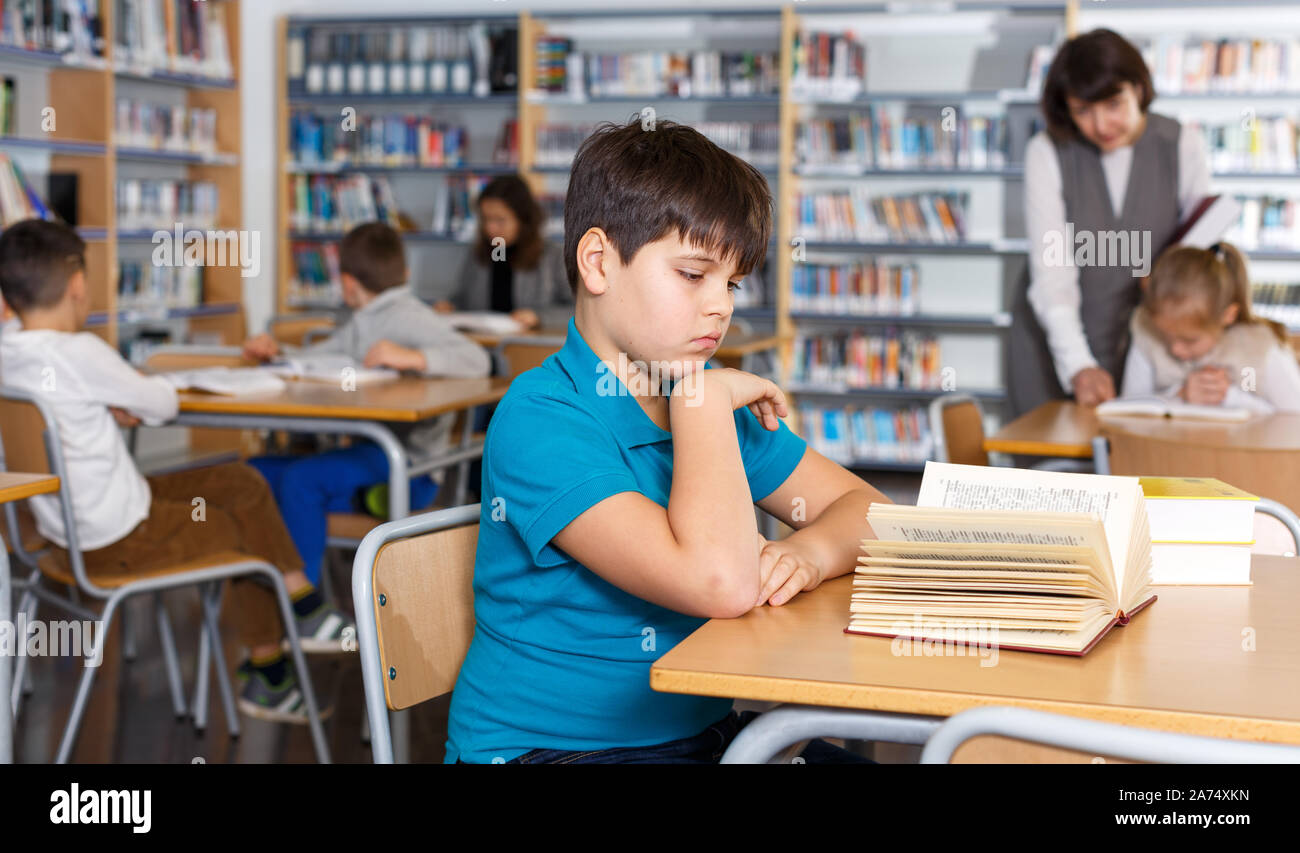 Focused boy reading in school library on background with other students ...