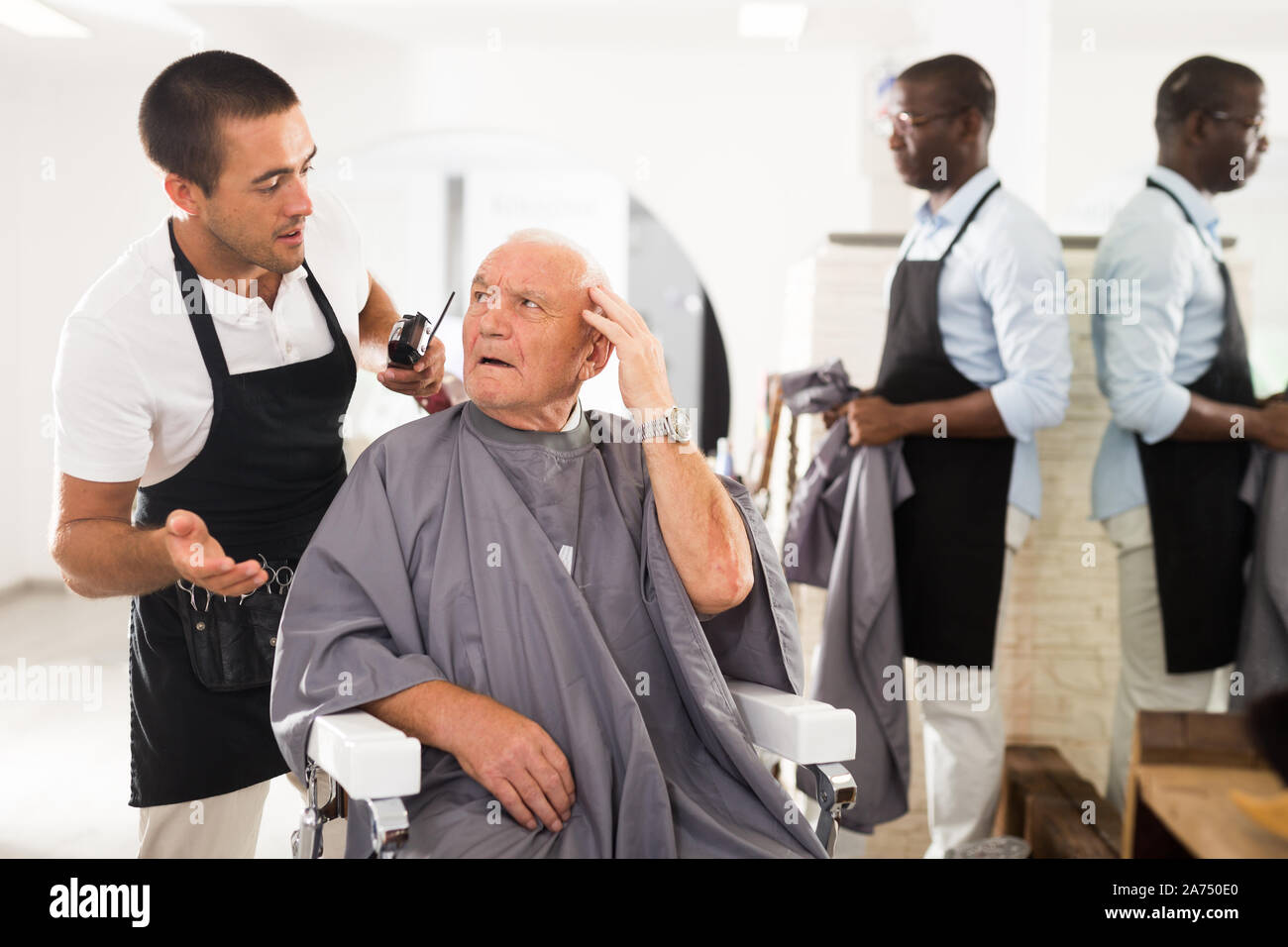 Portrait of shocked elderly man sitting in barber chair with confused ...