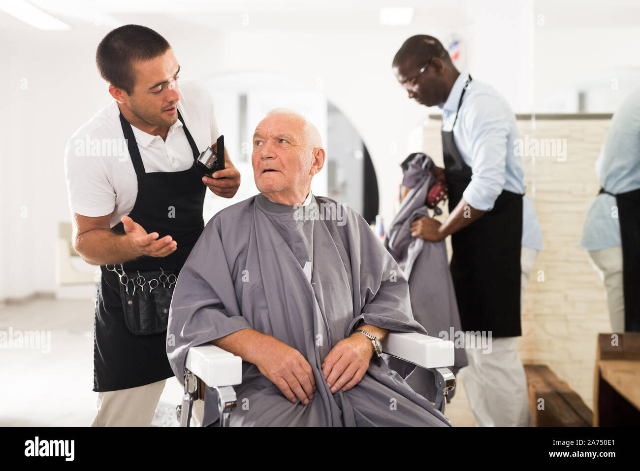 Portrait of shocked elderly man sitting in barber chair with confused ...