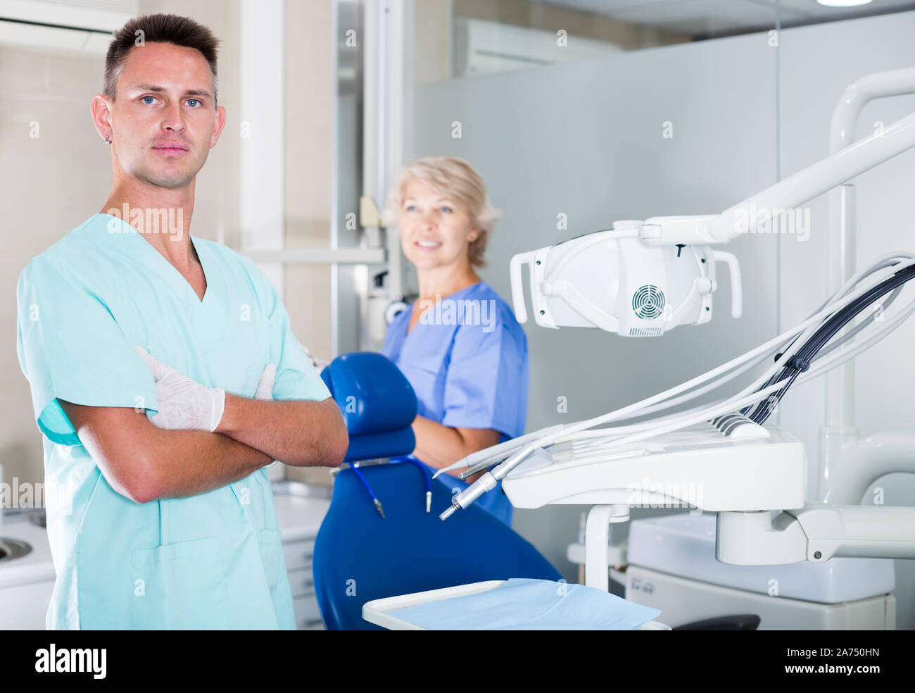 Male dentist standing in dental office with hands crossed looking at ...