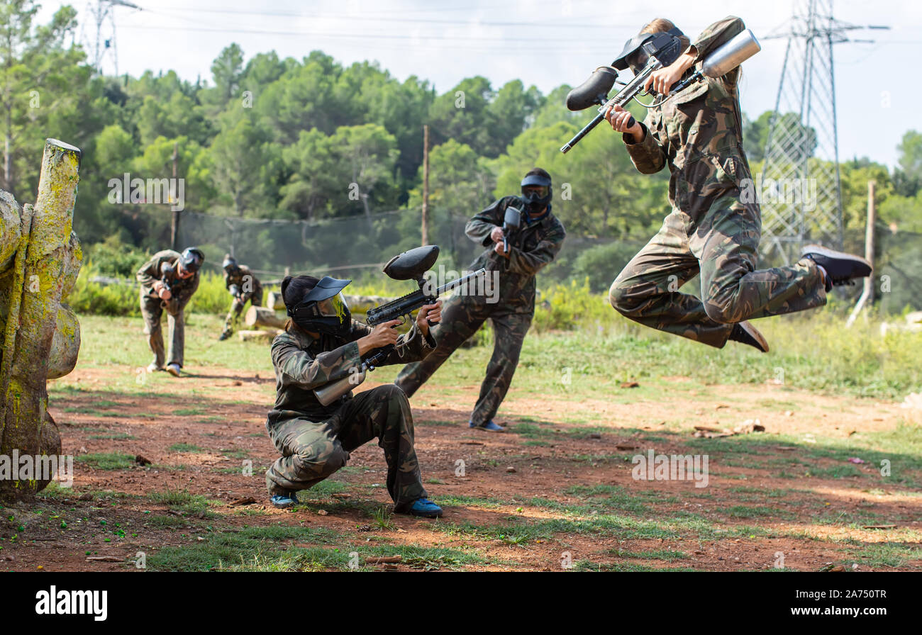 Dynamic paintball battle. Portrait woman player jumping and aiming marker on member of opposing ...
