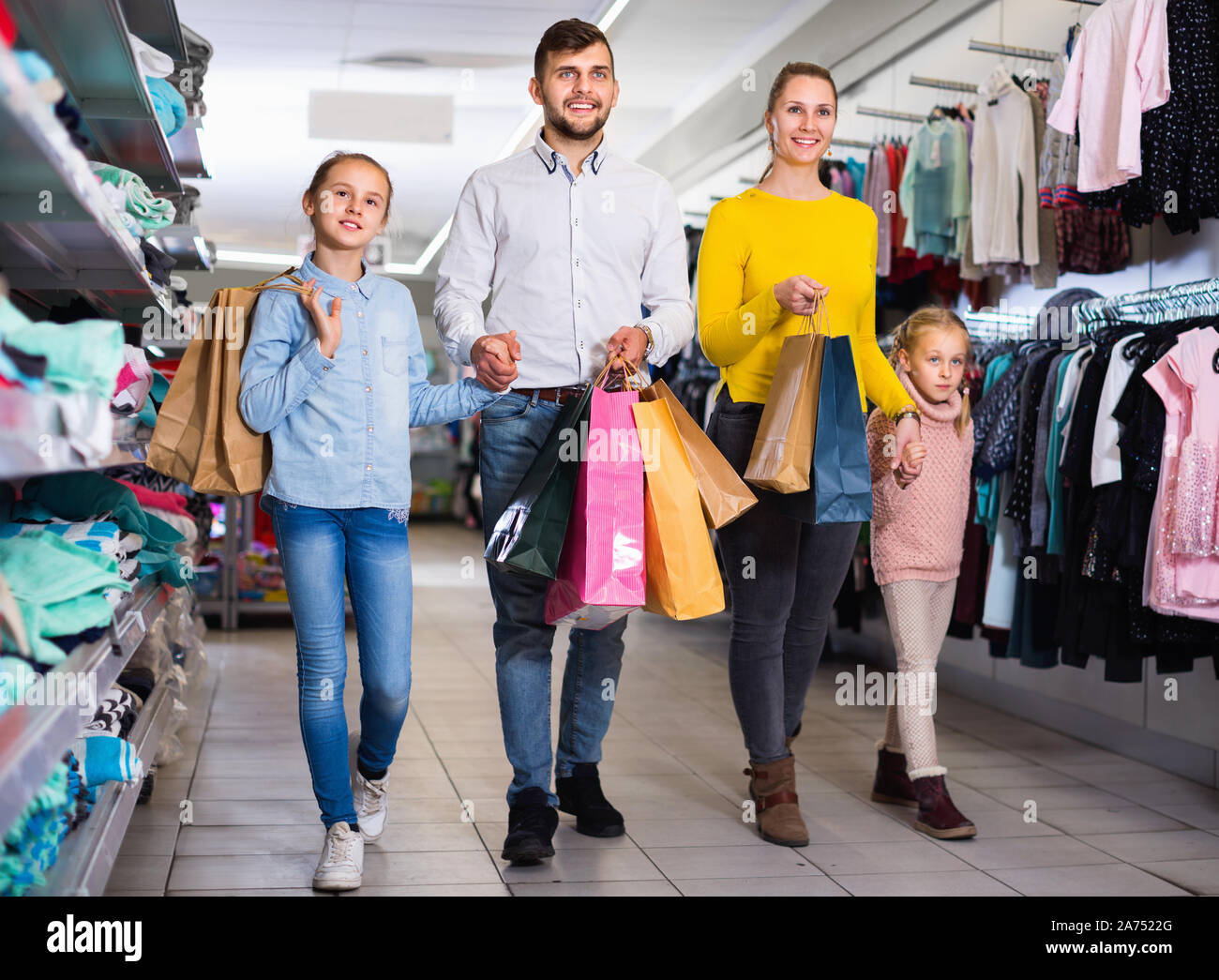 Young happy cheerful parents with two little girls shopping in mall ...