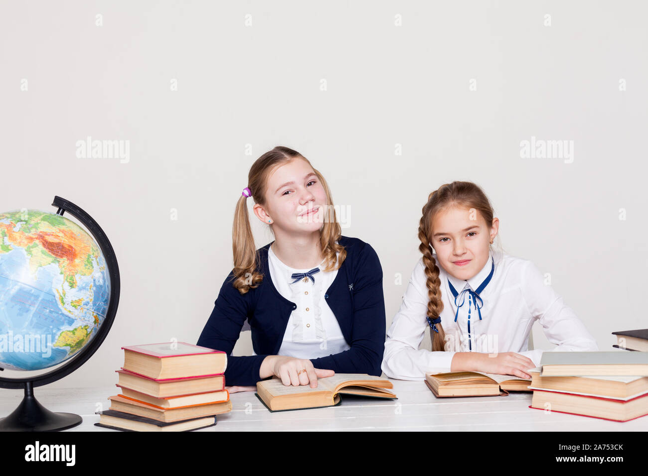 two girls with books and a globe in class at the desk at school Stock ...