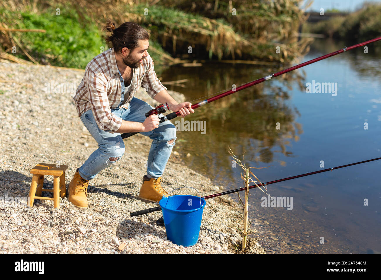 Adult man standing near river and pulling fish expressing emotions of ...