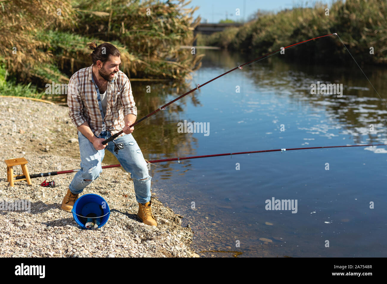 Adult man standing near river and pulling fish expressing emotions of ...