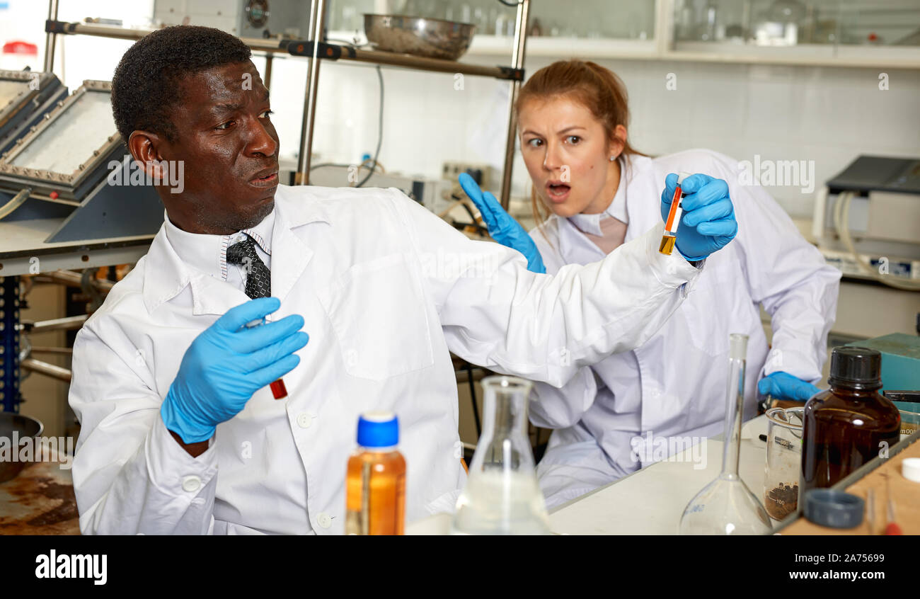 Serious male scientist with test tubes checking for result of chemical ...
