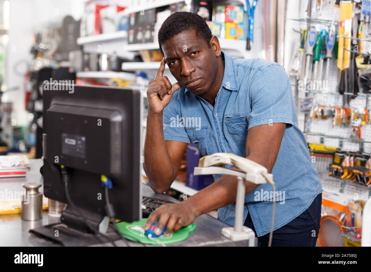 Positive African American salesman working on computer behind counter ...