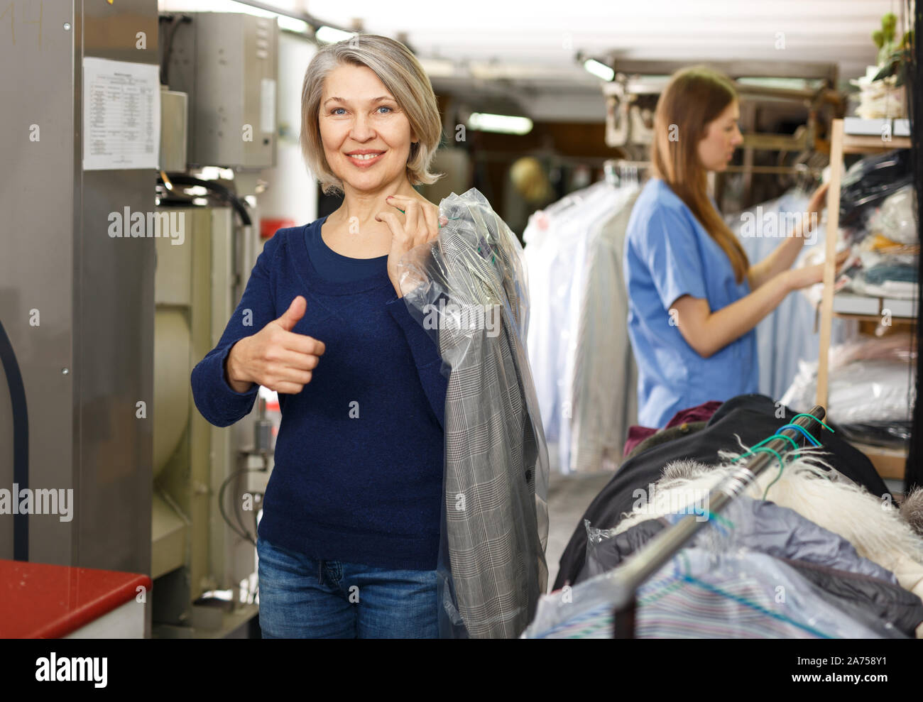 Portrait of satisfied female customer holding her clean clothes at dry ...