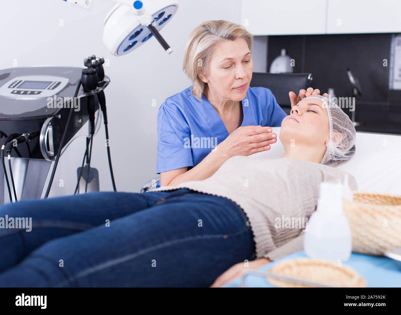 Professional cosmetician examining face skin of girl in clinic of ...