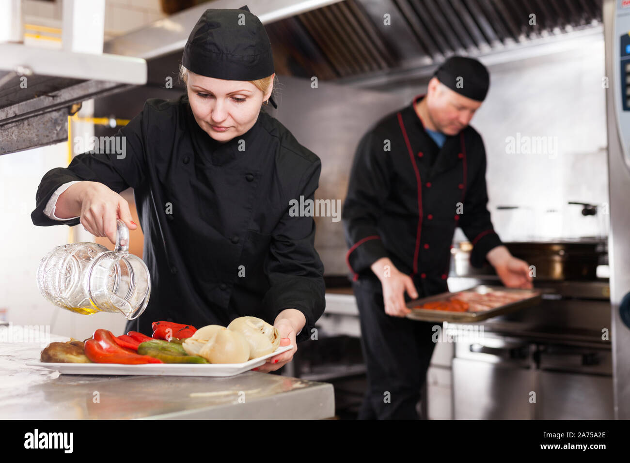 Skilled female chef seasoning finished dish with olive oil before ...
