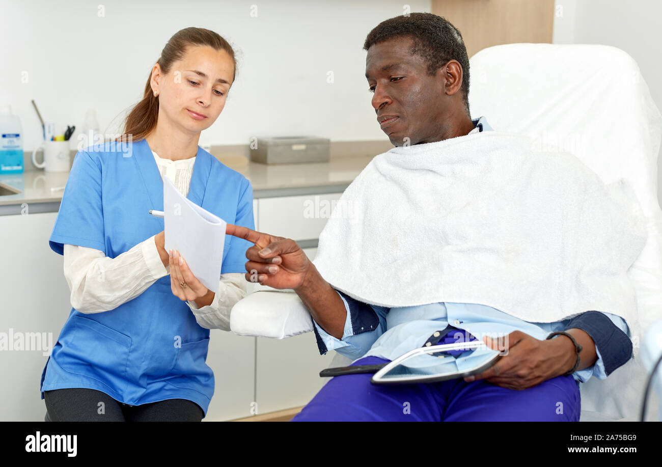 Professional cosmetician woman with papers talking to man before ...